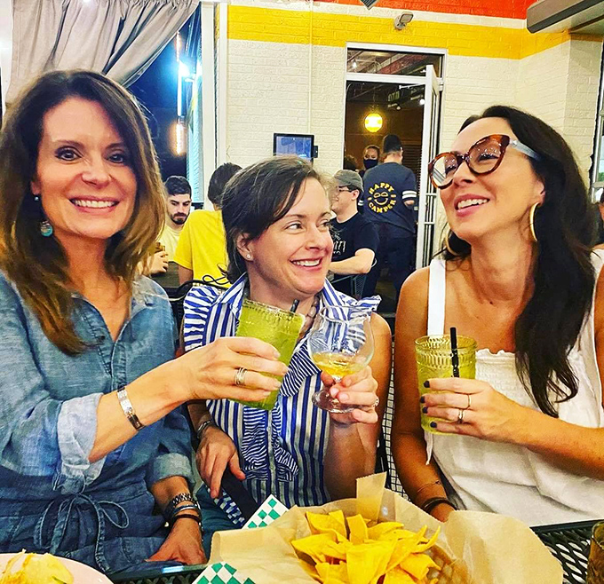 Three friends raising colorful drinks in a toast to good times. The chips might be on the table, but the real gold is in those glasses.