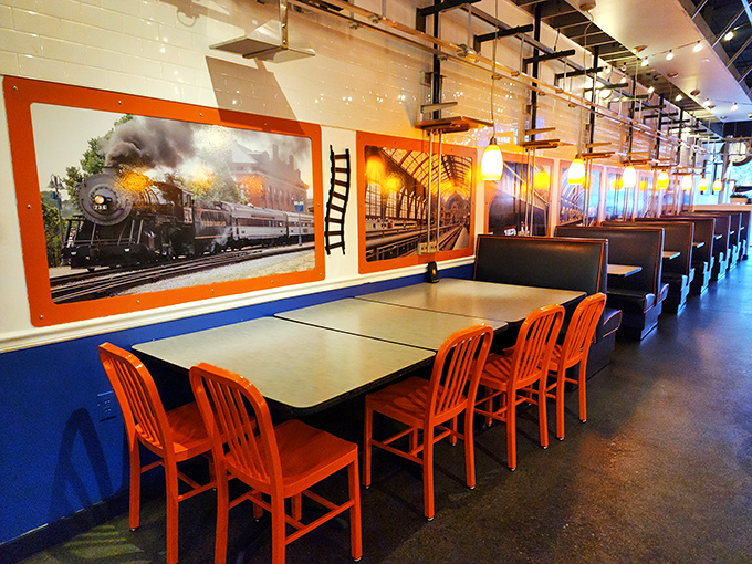 Bold orange chairs pop against blue walls adorned with vintage train artwork. The dining area feels like stepping into a stylish railway car from a more civilized era.