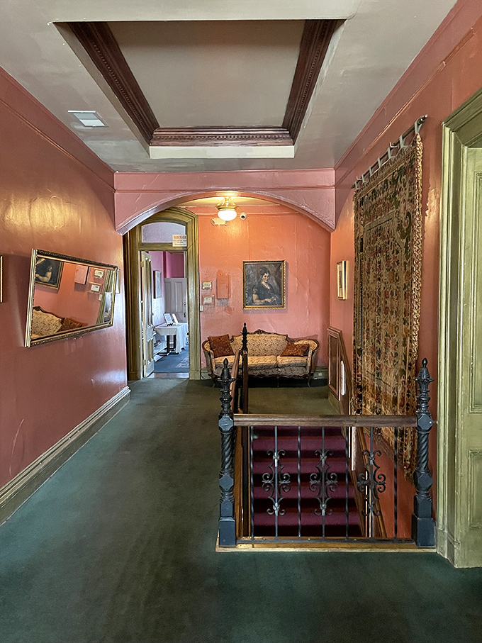 The salmon-colored hallway connects rooms where tragedy once unfolded. Those vintage railings have supported hands from both this world and perhaps the next.
