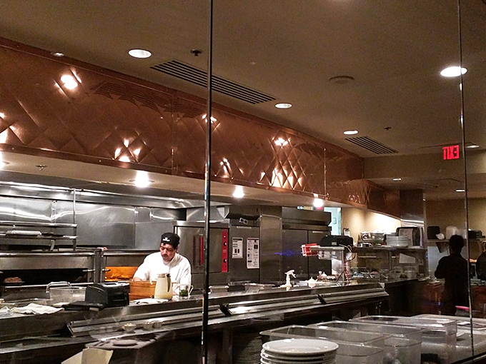 Behind the glass, culinary magic happens. The kitchen's copper accents reflect the serious business of transforming prime beef into memorable meals.