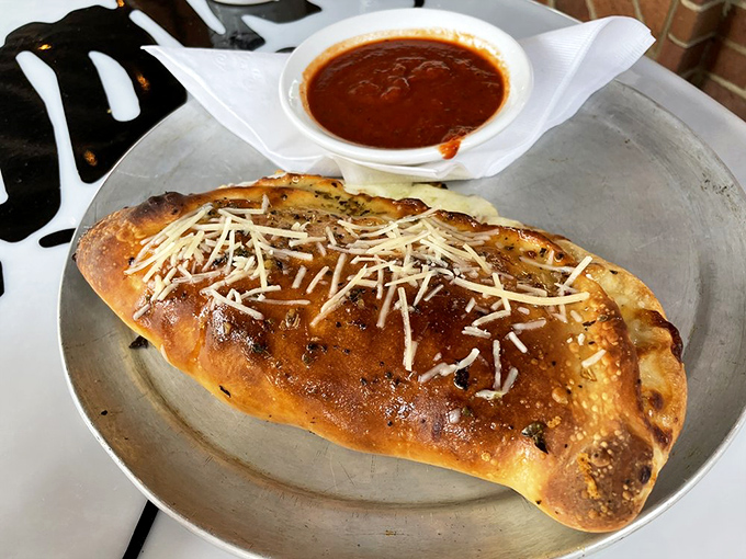 The calzone arrives looking like an edible treasure chest, golden-brown and bursting with cheese treasures that would make any pirate weep.