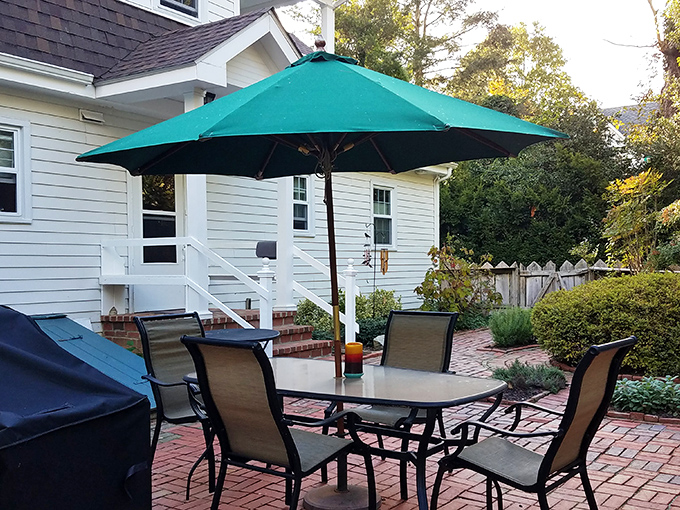 The backyard patio setup practically whispers, "Your afternoon plans are canceled. You live here now, under this umbrella, with these comfortable chairs."