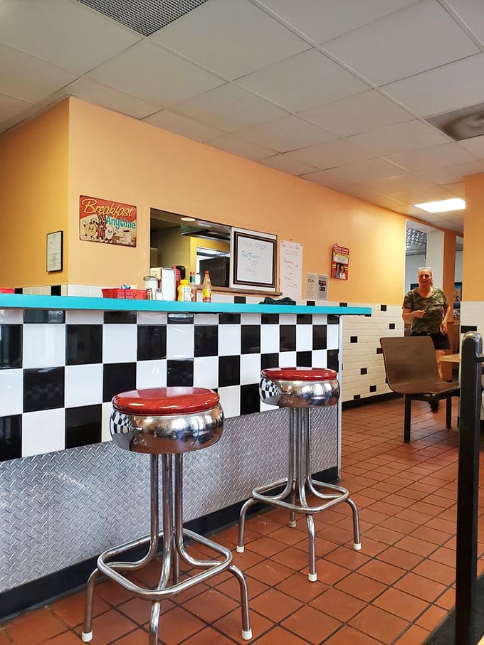 The counter area with its classic checkered pattern and chrome stools invites solo diners to perch and watch the breakfast ballet unfold in the kitchen.