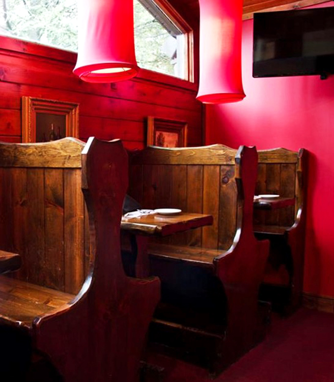 Church-pew inspired booths against crimson walls create intimate dining nooks where confessions of food love are whispered daily.
