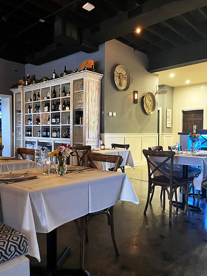 Wine bottles stand at attention like soldiers guarding flavor treasures. The rustic-meets-refined aesthetic creates the perfect backdrop for serious dining without the stuffiness.