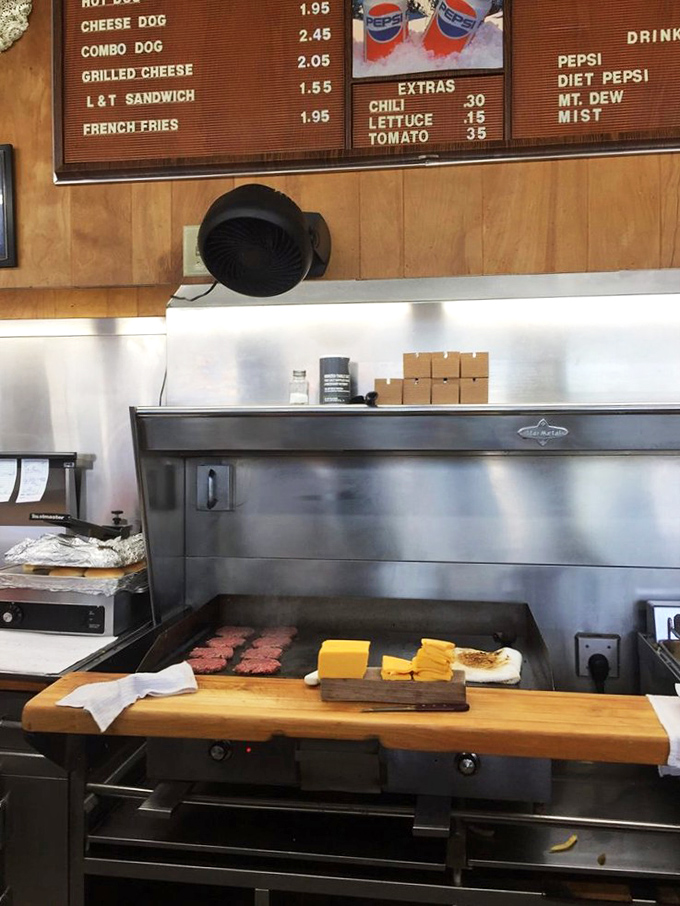 The moment of creation: fresh patties hit the seasoned grill while blocks of cheese await their moment to transform ordinary beef into extraordinary burgers.