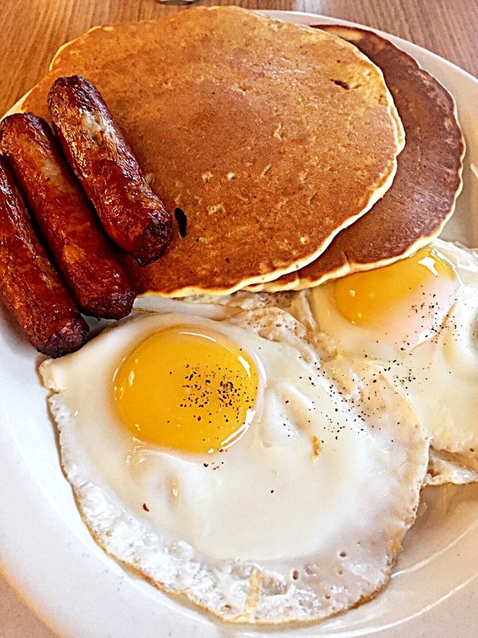 The breakfast trinity: golden pancakes, sunny-side-up eggs with perfect yolks, and sausages that deserve their own fan club.