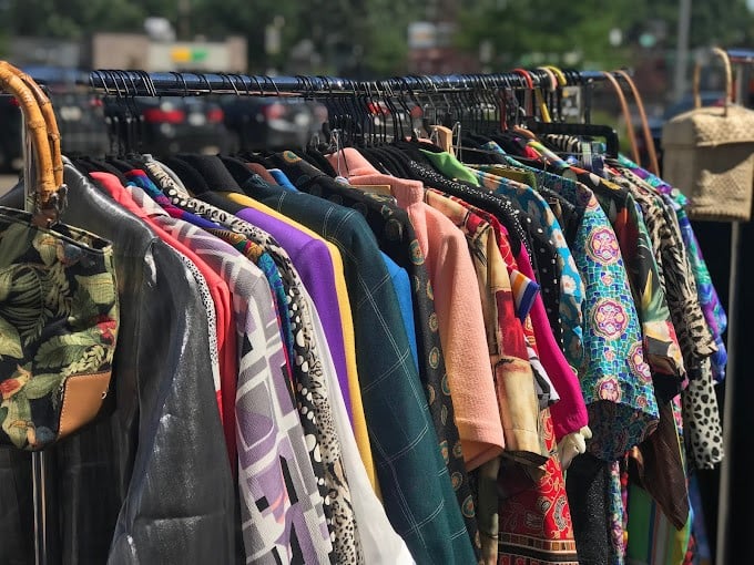 Sunlight streams through outdoor racks during seasonal sidewalk sales, where patterns and colors compete for attention like flowers in a garden.