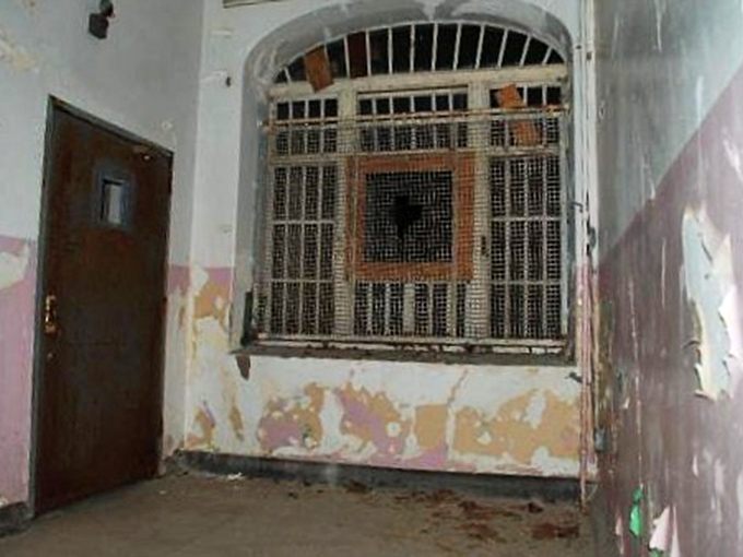 The security station's mesh window served as the boundary between freedom and confinement. Peeling paint reveals layers of institutional colors that marked passing decades.