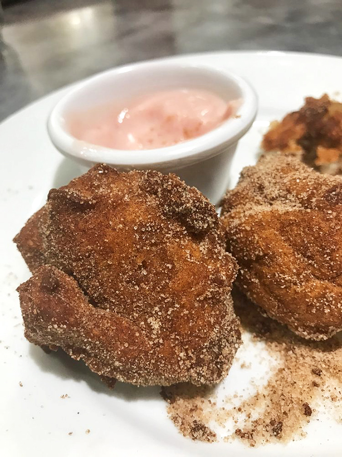 These aren't just apple fritters &ndash; they're cinnamon-sugar coated portals to happiness with a side of pink dipping sauce.