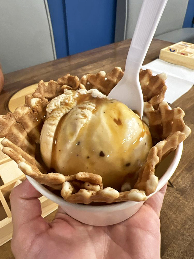 Golden waffle bowl cradles vanilla perfection drizzled with caramel. Spoon poised for that perfect first bite.