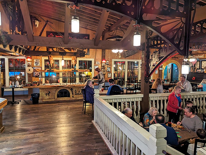 Dining areas divided by wooden railings create cozy nooks while maintaining the open, communal feeling of a frontier gathering.