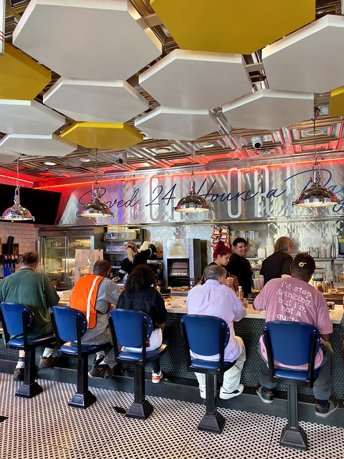 The counter experience – where regulars perch on blue stools beneath honeycomb ceiling panels, watching breakfast magic happen in real time.