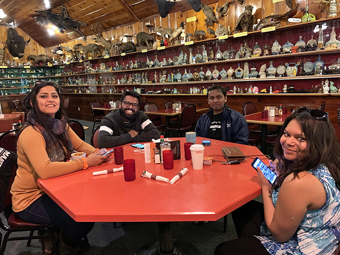 Four smiling diners surrounded by the restaurant's legendary bottle collection &ndash; proof that good food creates the best kind of community.