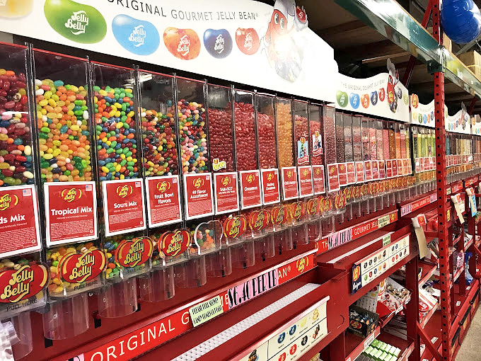 Jelly Belly dispensers stand like colorful sentinels, guarding flavors from the mundane to the magnificently bizarre. 