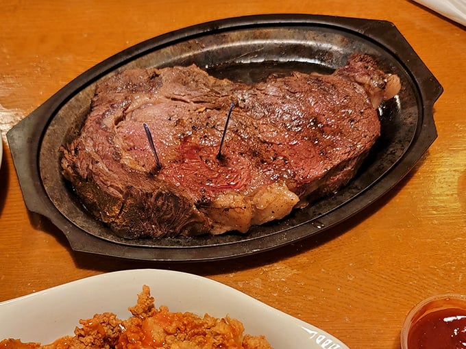 The prime rib arrives like royalty on a sizzling platter, its perfectly pink interior promising flavor that fancy city steakhouses charge double for.