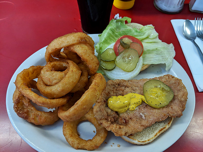 The perfect pork tenderloin sandwich&mdash;breaded, fried, and hanging off the plate as Indiana law requires. Those onion rings aren't just sides, they're supporting actors.