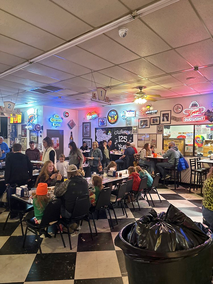 Families gather around tables in a room humming with conversation. The checkered floor has witnessed countless celebrations, all centered around fried chicken.