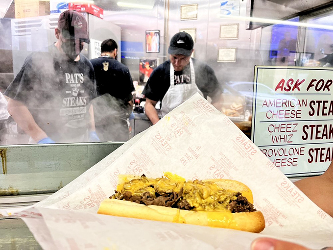 Behind the counter where legends are made. Pat's grill masters work their magic through a haze of steam, transforming simple ingredients into iconic meals.