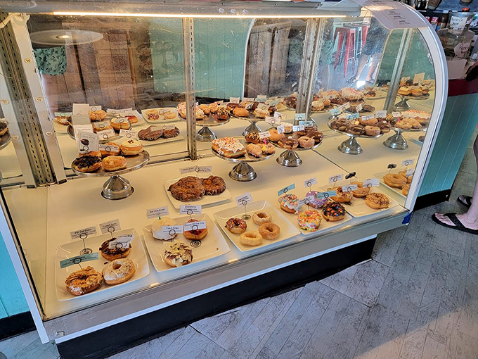 The display case&mdash;a museum of donut artistry where each pedestal showcases masterpieces more tempting than any Renaissance painting.