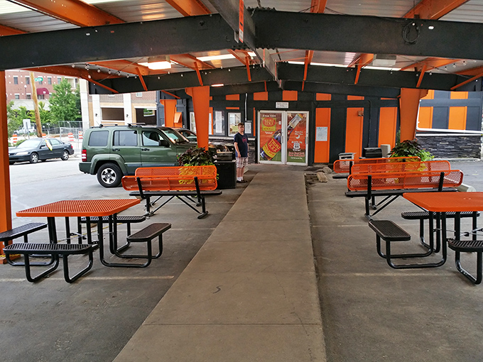 The outdoor seating area offers a perfect perch for people-watching, with signature orange tables that match the building's distinctive stripes.