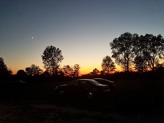 That magical twilight moment when day surrenders to night, silhouetting cars against a fiery sky as the screen awaits its time to shine.