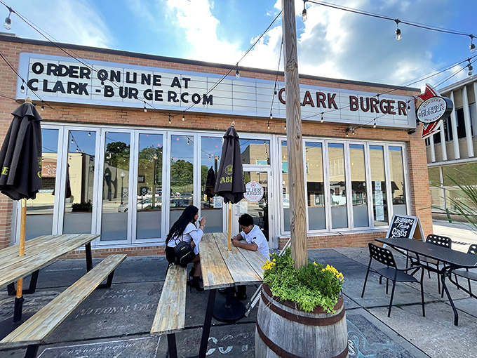Clark Burger's inviting patio welcomes burger enthusiasts with rustic wooden benches and twinkling string lights&mdash;a perfect urban oasis for beef bliss.