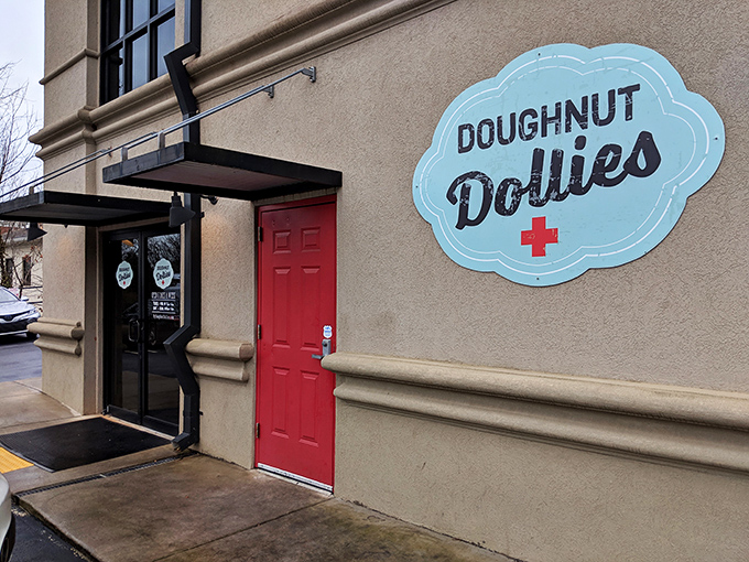 The iconic blue cloud sign of Doughnut Dollies against a beige wall with a cheerful red door. Simplicity that promises sweetness awaits inside!