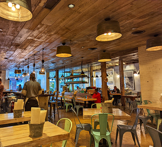 Rustic wooden ceilings, industrial lighting, and colorful metal chairs create a space that's both nautical and neighborly, like a fisherman's cabin with style.