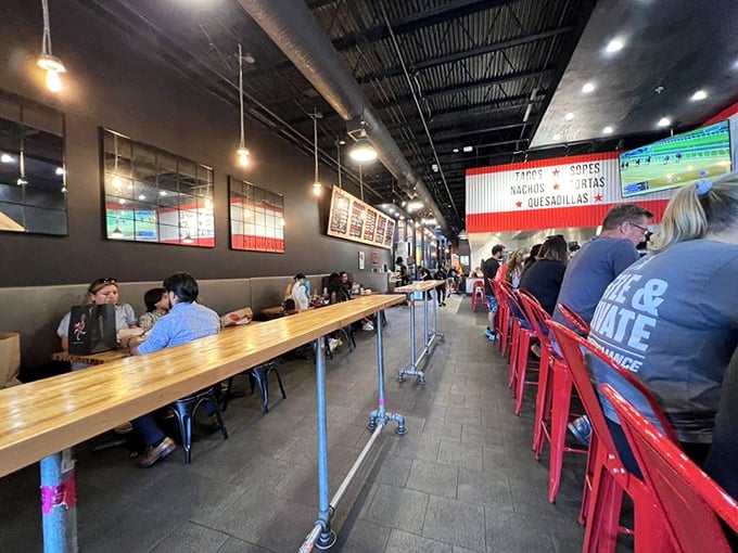 Industrial-chic meets taco paradise inside, where pendant lights dangle like culinary constellations over communal tables and those signature red stools.