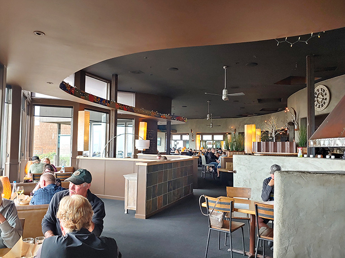 The warm wooden ceiling arches like an upturned boat hull, creating an intimate dining atmosphere even as the ocean stretches endlessly beyond the windows. 