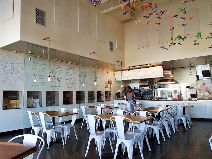 High ceilings adorned with colorful origami birds create an airy atmosphere where waffle dreams take flight. Industrial-chic meets breakfast paradise.