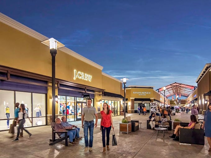 As evening falls, the outlets transform into a lively shopping village where couples hunt for deals under the warm glow of storefront lighting.