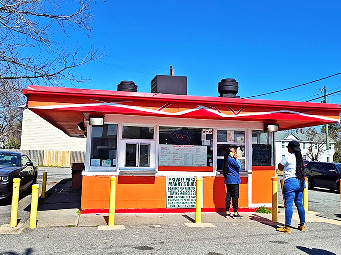 Manny's vibrant orange-and-red stand pops against the blue sky like a burger oasis. This Norfolk treasure proves great things come in small, colorful packages.