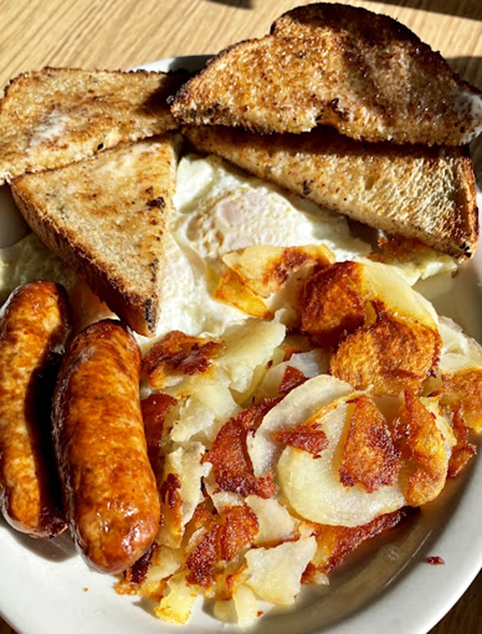 Breakfast's holy trinity: perfectly fried eggs, golden home fries with crispy edges, and sausage links that snap with each bite. The breakfast gods are smiling.