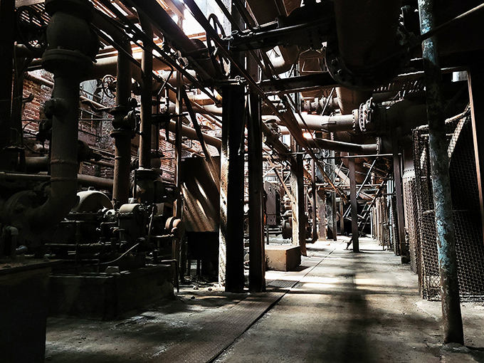 A solitary figure navigates the industrial labyrinth, dwarfed by rust-colored pipes that once channeled the lifeblood of Birmingham's economy.