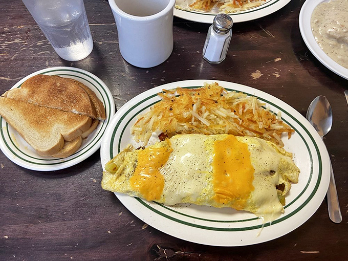Behold the omelet that requires commitment! Melted cheese cascades over eggs stuffed with breakfast treasures, with hash browns standing guard nearby.