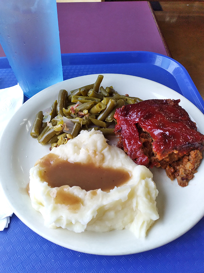 The holy trinity of Midwest comfort: meatloaf glazed to perfection, green beans with bacon, and mashed potatoes cradling gravy like an old friend.