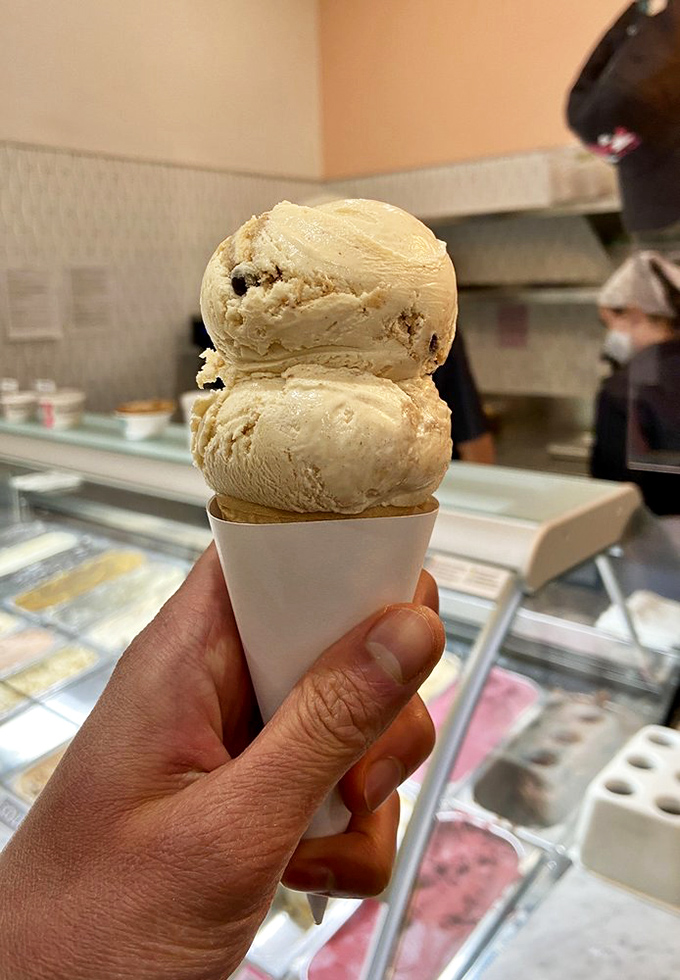 Two perfect scoops standing tall in a paper cone. This isn't just dessert; it's edible architecture that demands to be admired before devoured.