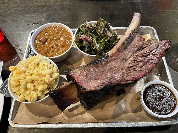 Behold the holy trinity of barbecue bliss: a beef rib that Fred Flintstone would envy, mac and cheese that hugs your soul, and greens that make virtue taste sinful.