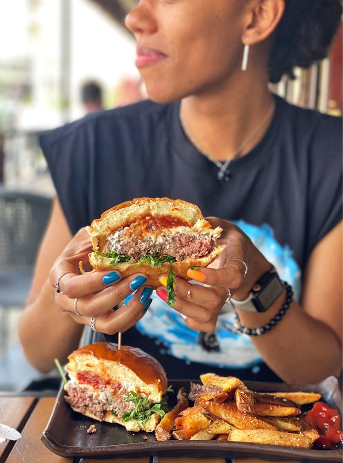 A perfectly medium burger revealing its pink soul, held by colorful fingernails that know they're about to experience something transcendent.