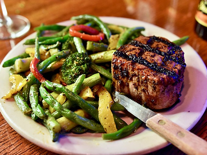 A perfectly char-grilled filet nestles alongside garden-fresh vegetables, proving that simple preparations often create the most profound pleasures.