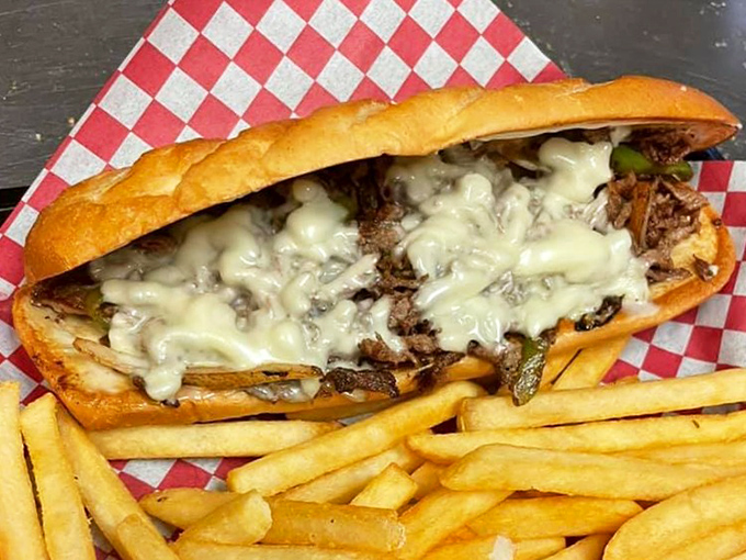 Behold the cheesesteak in its natural habitat—nestled on checkered paper, oozing with cheese, and flanked by golden fries. Resistance is futile.
