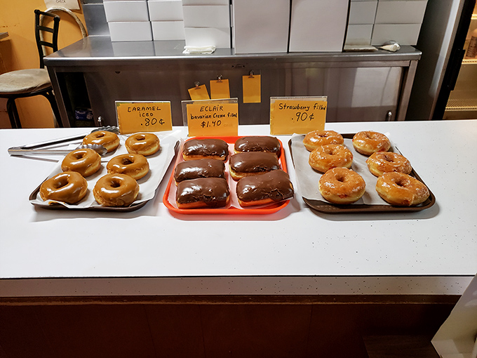 The holy trinity of donut perfection: caramel-glazed, chocolate-covered eclairs, and strawberry-filled treasures, all displayed with unpretentious pride.