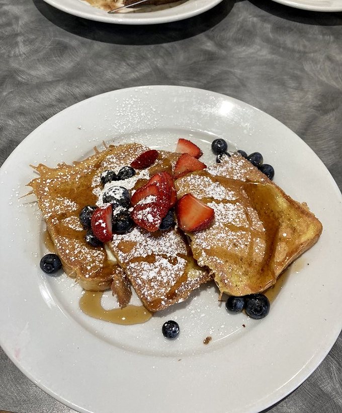 French toast nirvana achieved: golden slices adorned with fresh berries and a snowfall of powdered sugar that would make Elsa jealous.