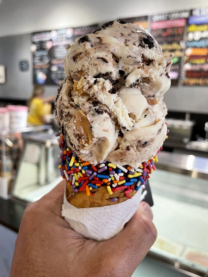 Ice cream architecture at its finest&mdash;cookie chunks and caramel ribbons balanced precariously on a rainbow-sprinkled cone that demands immediate attention.