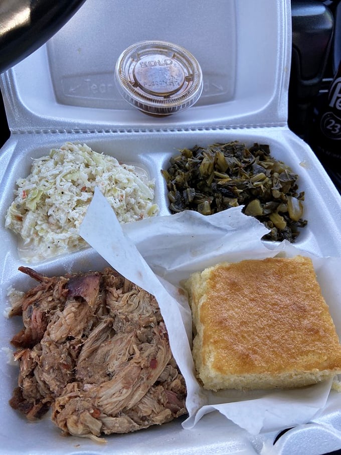 Behold the holy trinity of Southern comfort: pulled pork, coleslaw, and collards, with cornbread standing by as the faithful sidekick. Styrofoam never held such treasure.