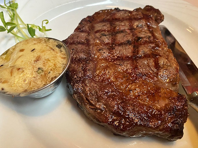 Behold the ribeye in its natural habitat – perfectly seared, seasoned with reverence, and accompanied by a sauce that should have its own fan club.