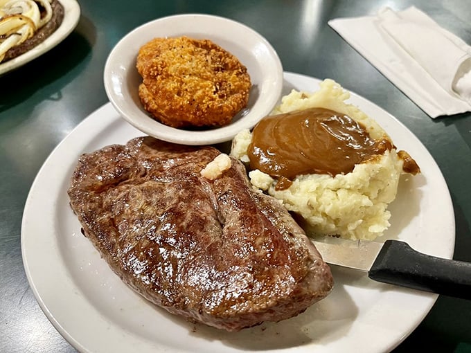 This isn't just steak &ndash; it's a carnivore's dream vacation. Perfectly grilled, accompanied by a golden-brown onion ring and mashed potatoes swimming in gravy.