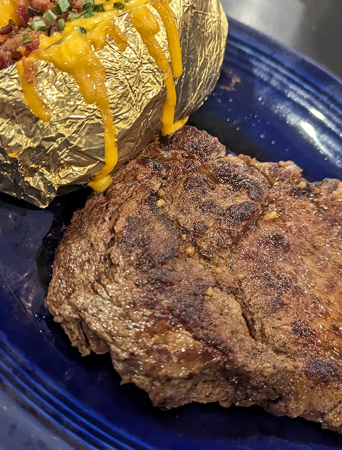 This steak doesn't need fancy presentation—it speaks the universal language of perfectly seasoned beef. That loaded potato is practically doing a victory lap alongside it.